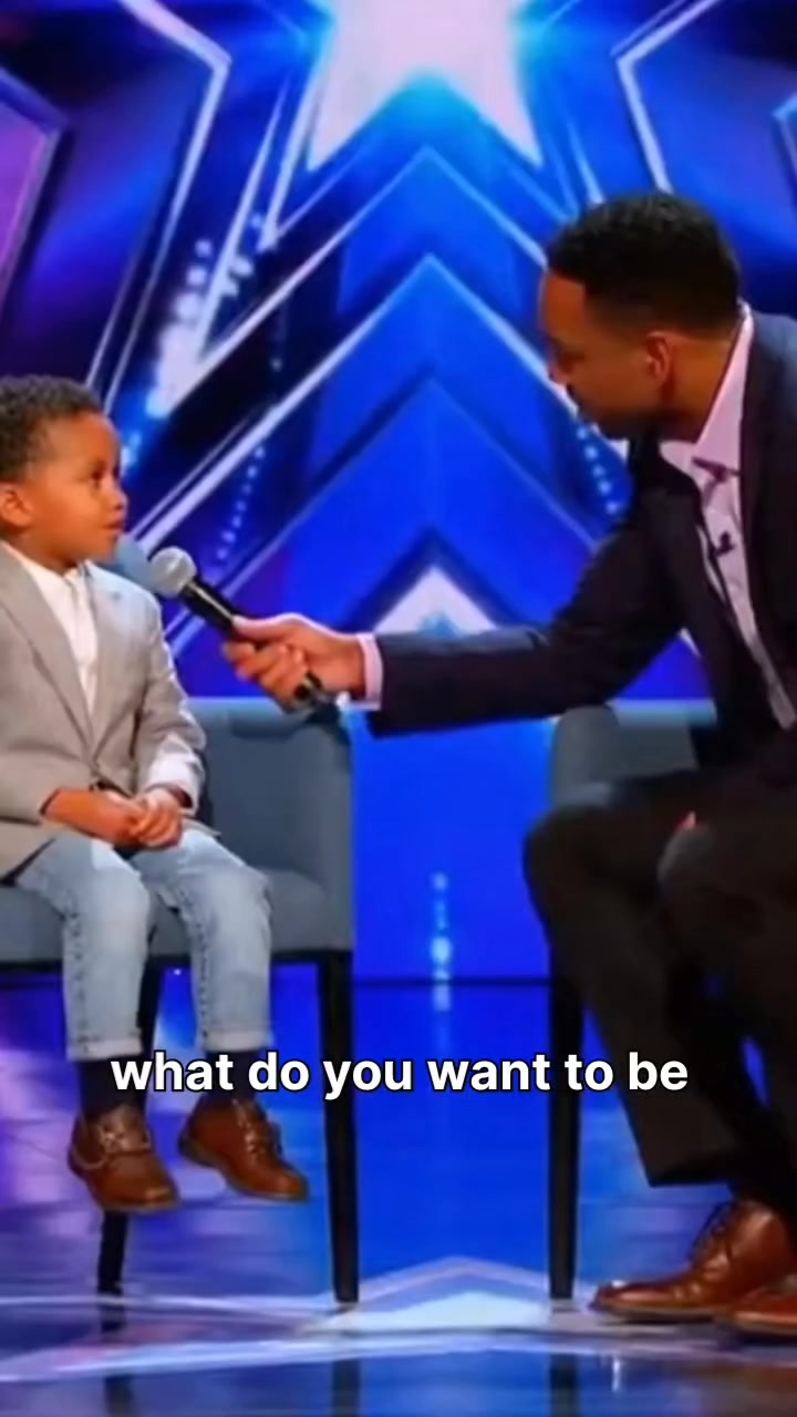 On a brightly lit theater stage, a 4-year-old boy answers a simple ...